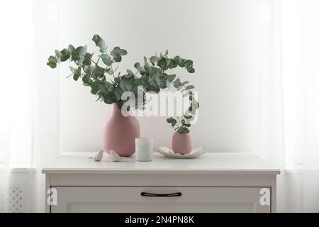 Chest of drawers with candle and eucalyptus branches near light wall ...