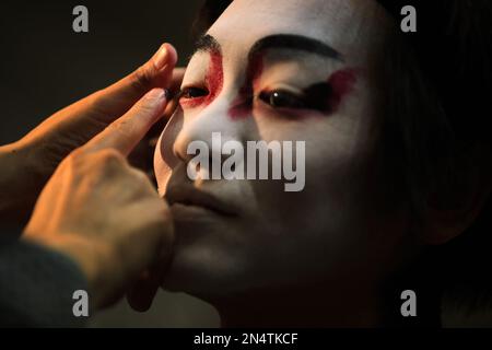 A professional artisan of kabuki makeup paints a man's face with a ...