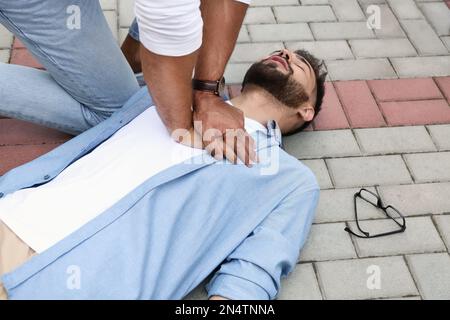 Passerby performing CPR on unconscious young man outdoors. First aid ...
