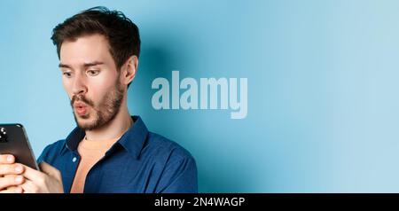 Image of impessed young man looking at smartphone and saying wow ...