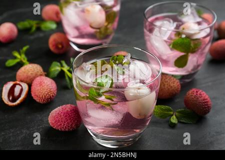 Delicious lychee cocktails with mint and fresh fruits on black table ...