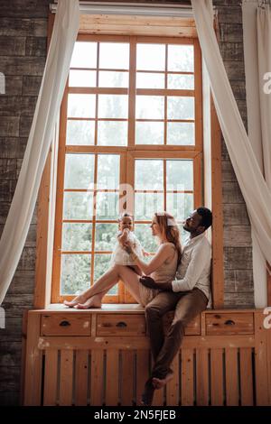 mother near happy infant daughter looking at camera in bedroom, banner ...