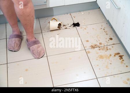 Woman standing next to broken tea cup laying on the kitchen floor ...