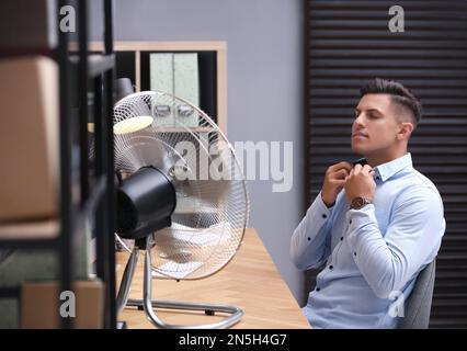 Man enjoying air flow from fan at workplace Stock Photo - Alamy