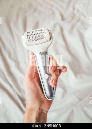 Woman holds epilator on crumpled bed background. Epilation ...