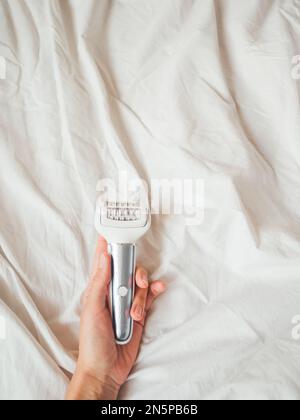 Woman holds epilator on crumpled bed background. Epilation ...