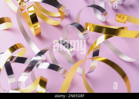 Shiny serpentine streamers on lilac background, closeup. Space for text ...