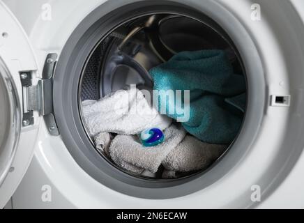 Laundry detergent capsule and towels in washing machine drum, closeup ...