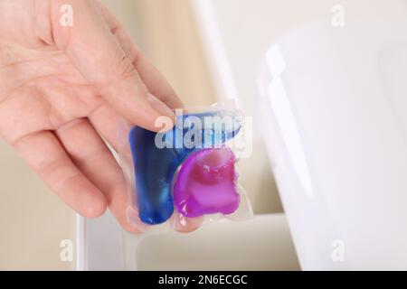 Woman putting laundry detergent capsule into washing machine indoors ...