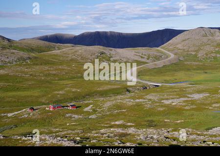 Green land with barren, stony mountains and a lake, single cabins ...