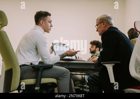 Senior male guiding and tutoring the new young employee at the office ...