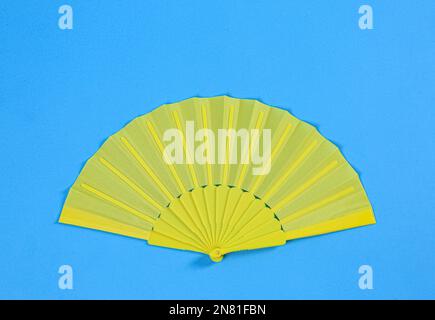 Yellow hand fan on light blue background, top view. Space for text ...