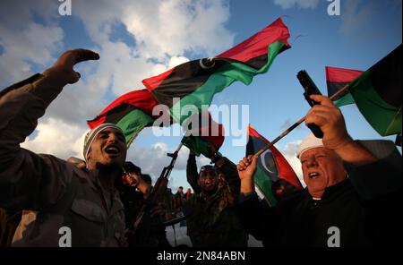 Libyans wave the national flags as they chant pro-revolutionary slogans ...