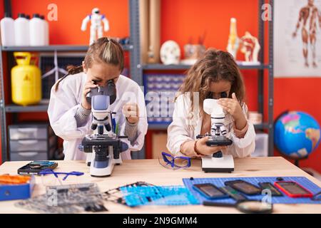 Two kids students using microscopes standing at laboratory classroom ...