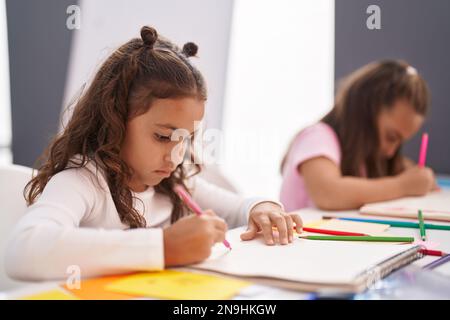 Adorable hispanic boy student sitting on table drawing on paper at ...