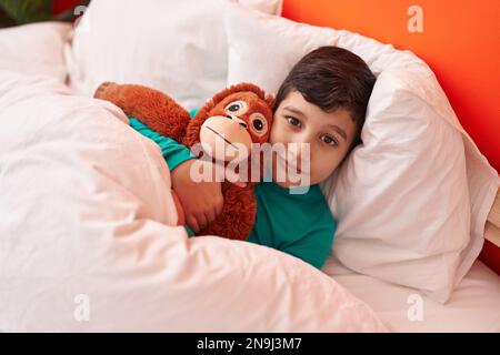Adorable hispanic boy hugging monkey doll lying on bed at bedroom Stock ...
