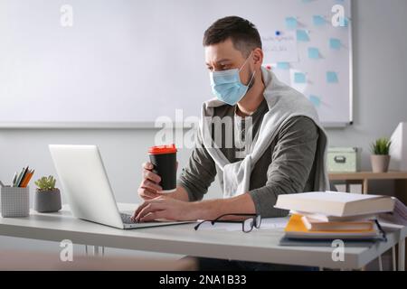 Teacher with protective mask conducting online lesson in classroom ...