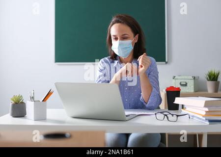 Teacher with protective mask conducting online lesson in classroom ...
