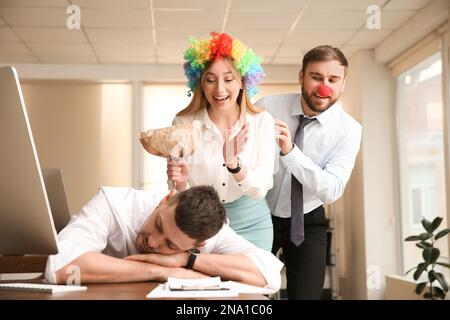 Coworkers popping paper bag behind their colleague in office. Funny ...