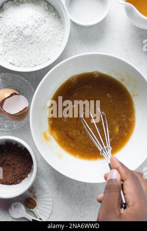 Overhead view of Whisking eggs and brown sugar in a white mixing bowl ...