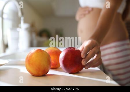 Young pregnant woman washing fresh sweet peaches in kitchen, closeup ...