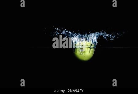 Ripe green apple falling down into clear water with splashes against ...