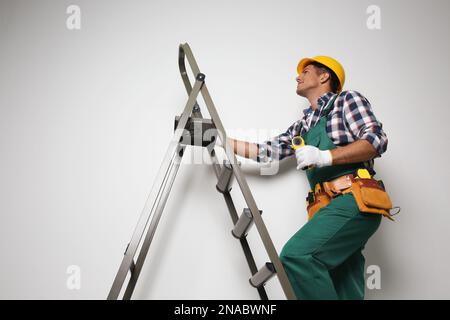 Professional builder climbing up metal ladder on white background ...