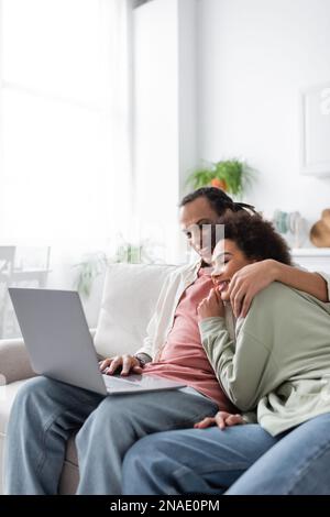 tattooed girlfriend hugging boyfriend while he using computer at home ...