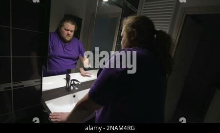 Upset man leaning on sink and looking in mirror at bathroom. Concept of ...