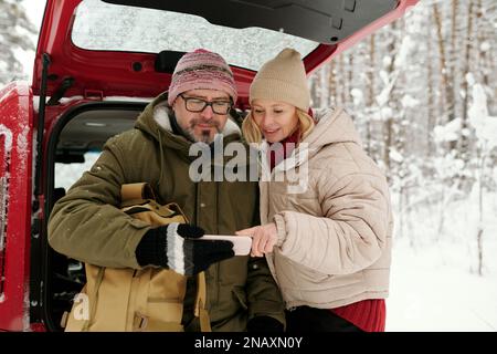 Happy mature woman with smartphone pointing at viewer on light blue ...
