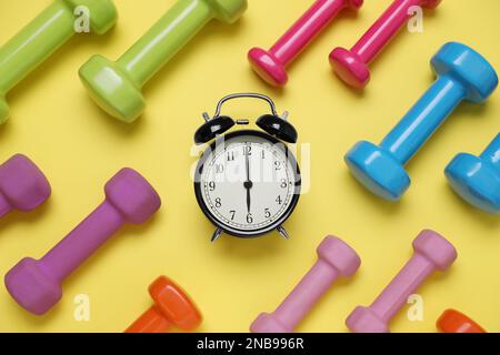 Yellow dumbbells and alarm clock on light blue background, flat lay ...