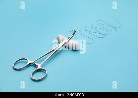 Forceps with suture thread and bandage roll on light blue background ...