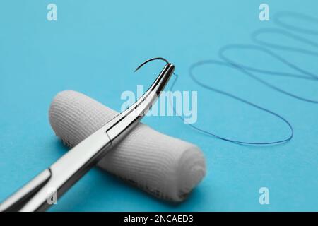 Forceps with suture thread and bandage roll on light blue background ...