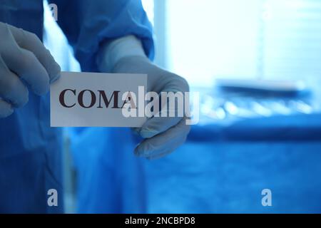 Surgeon holding card with word Coma in hospital, closeup. Space for ...