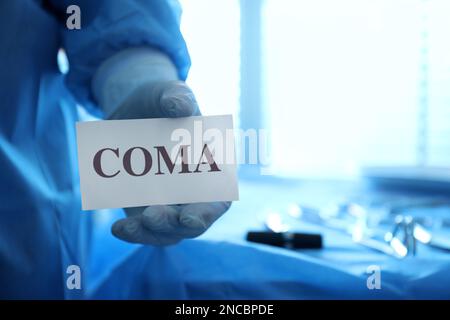 Surgeon holding card with word Coma in hospital, closeup. Space for ...