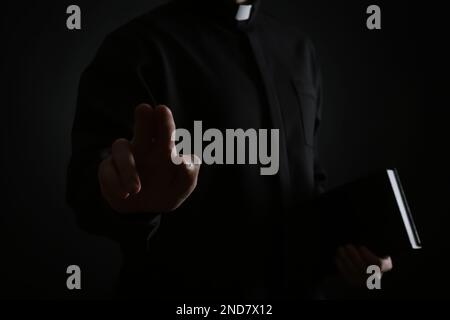 Priest with Bible making blessing gesture and holy light on dark ...