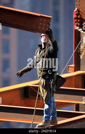 An ironworker guides a steel beam, suspended by a crane, into place at ...