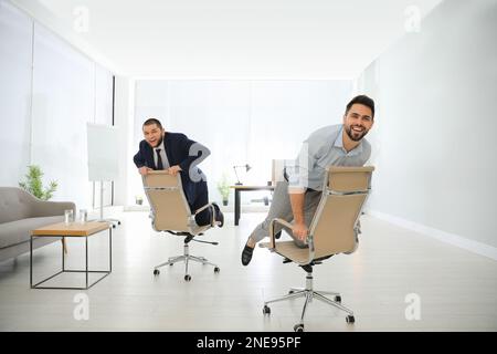 Happy office employees riding chairs at workplace Stock Photo - Alamy