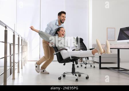 Office employee giving his colleague ride in chair at workplace. Space ...