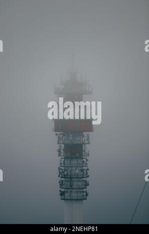 Telecommunication tower covered in the fog and clouds on a gloomy day ...