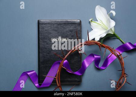 Holy Bible with purple ribbon, crown of thorns and lily flower on blue ...