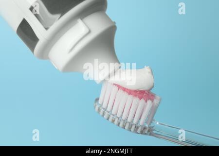 Squeezing toothpaste onto brush against light blue background, closeup ...