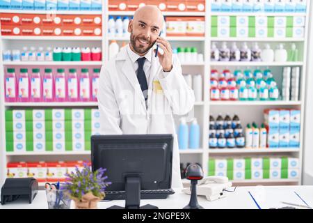 Young bald man pharmacist talking on smartphone writing on document at ...