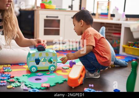 Teacher and toddler playing with cars toy sitting on table at ...