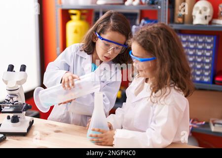 Two kids students pouring liquid on test tube at laboratory classroom ...
