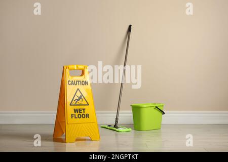 Safety sign with phrase Caution wet floor, mop and bucket indoors ...