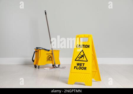 Safety sign with phrase Caution wet floor, mop and bucket on white ...