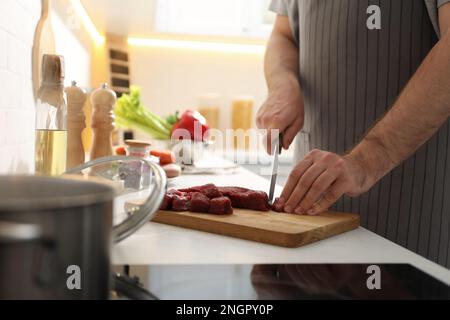 Man cutting meat to make bouillon in kitchen, closeup. Homemade recipe ...