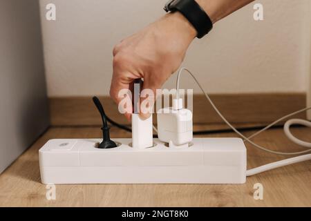 Human hand puts the charger into a filled extension cord. White cable ...