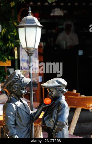 Statues of different gender in front of a restaurant holding a tomato ...